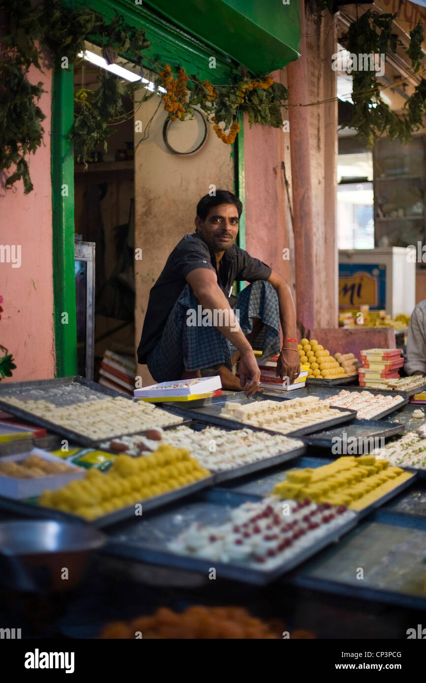 A man selling sweets on a stall in the back streets of a Jaipur bazaar ...