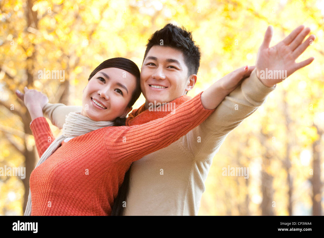 Young couple with arms outstretched, Autumn leaves in the background ...