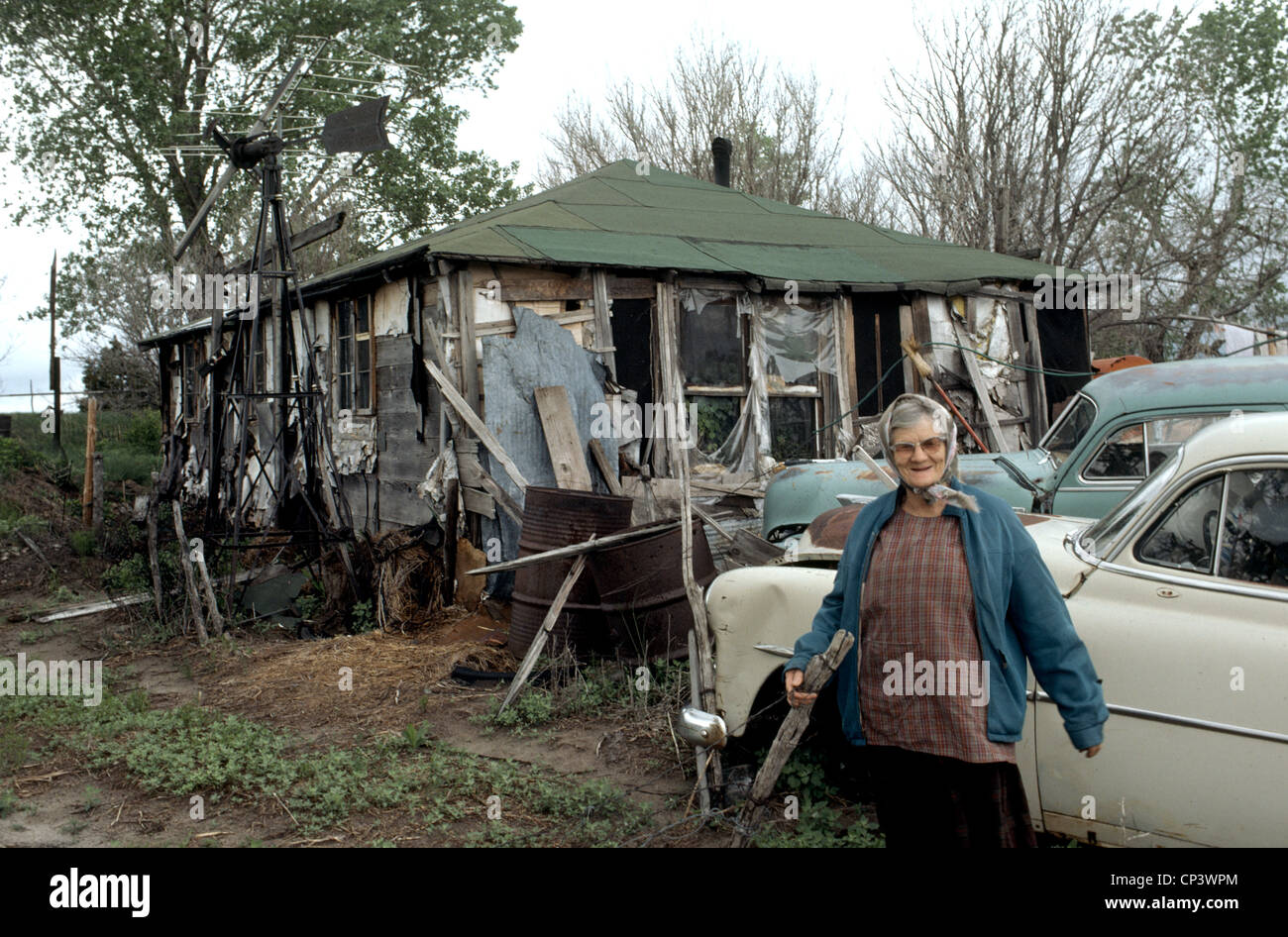 Old woman in front of her very poor dilapidated shack with old cars ...