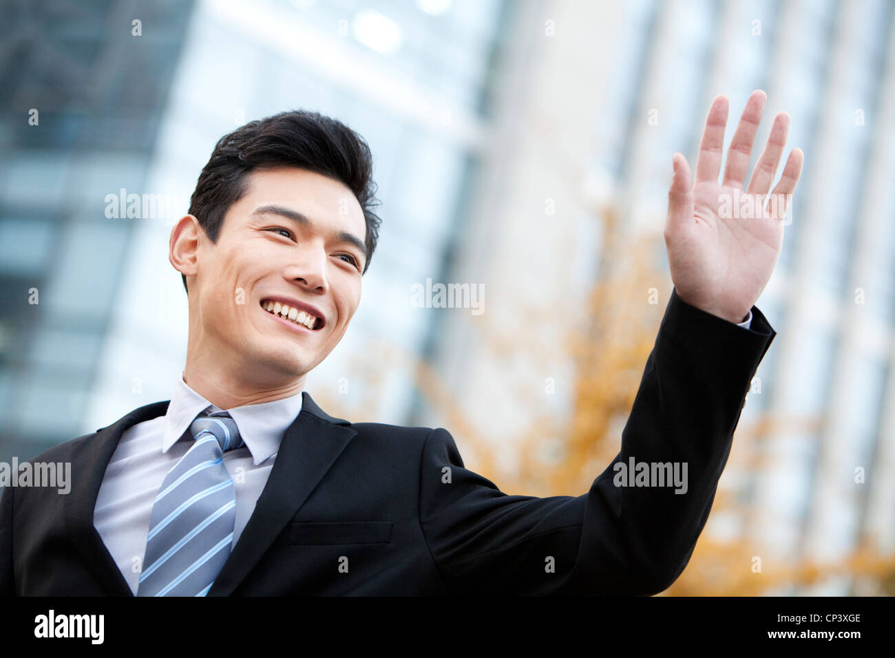 A businessman outside office buildings waving Stock Photo - Alamy