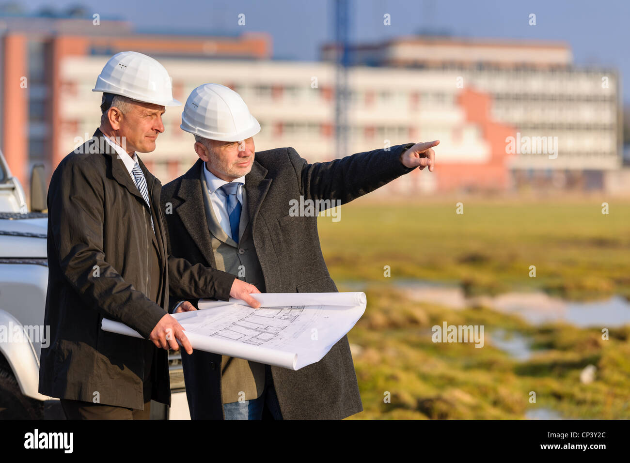 Two senior architect developers review plans at a construction site ...