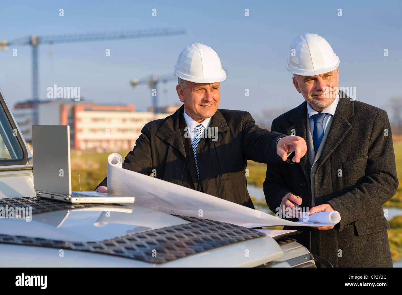 Male developers with blueprints at construction site discuss architect ...