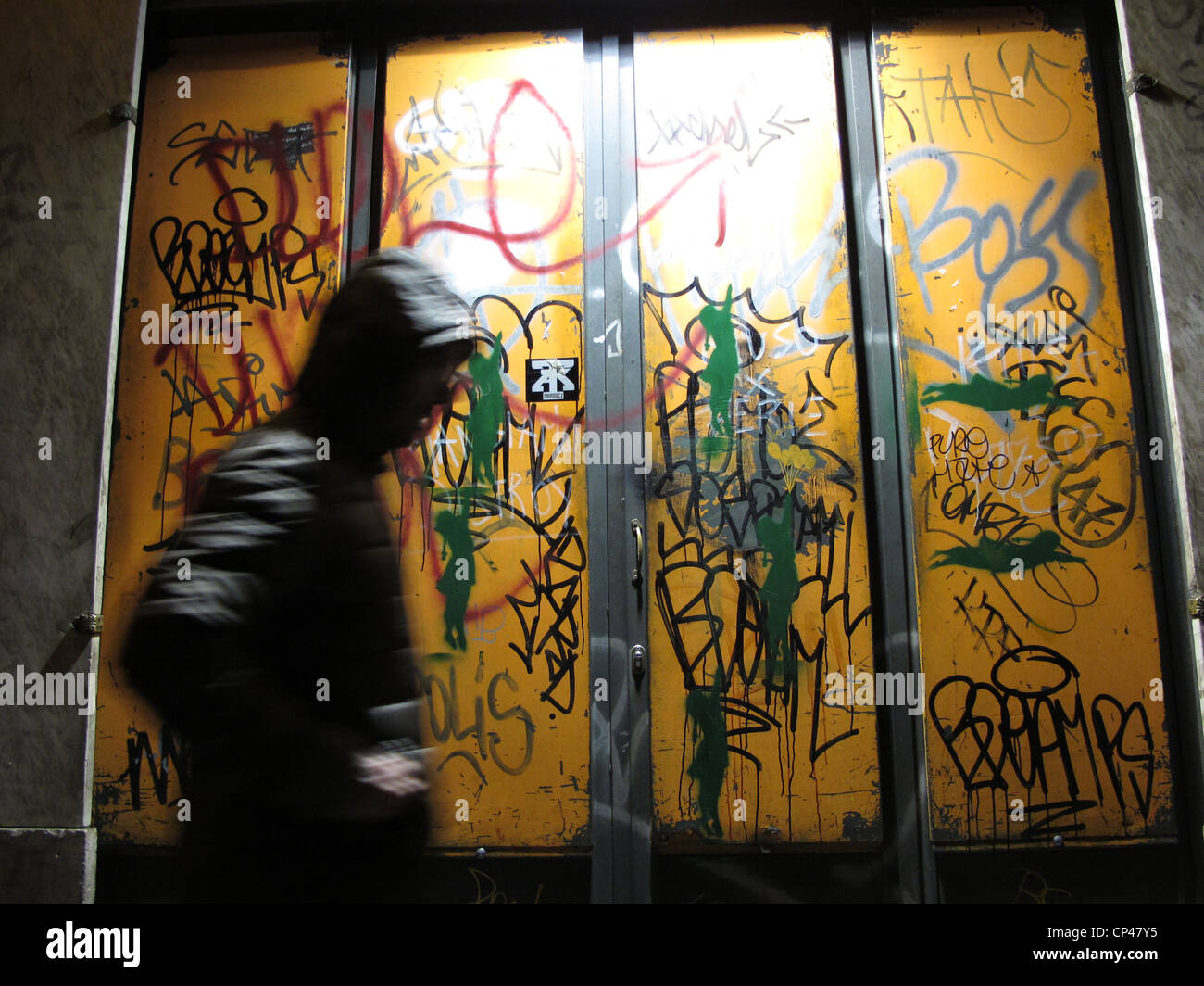 person walking past graffiti covered door in city at night Stock Photo ...
