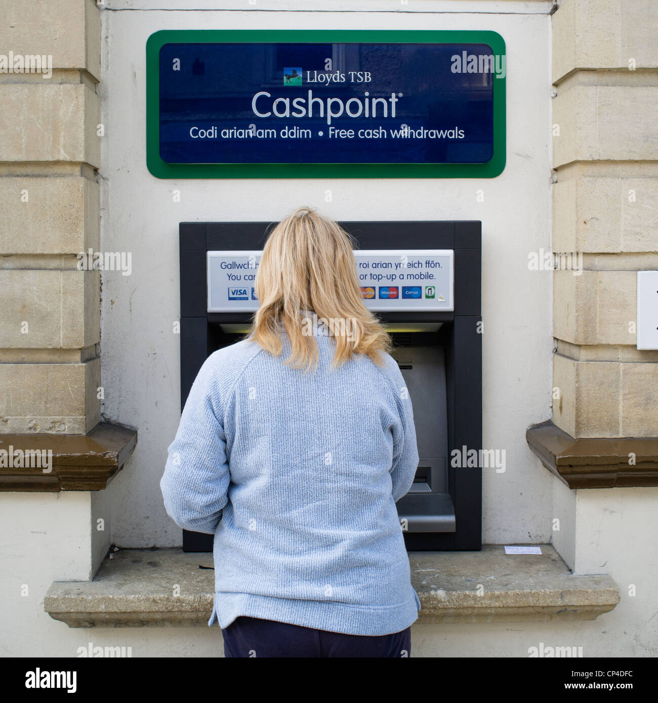 A rear view of a woman using a hole in the wall ATM Lloyds TSB bank ...
