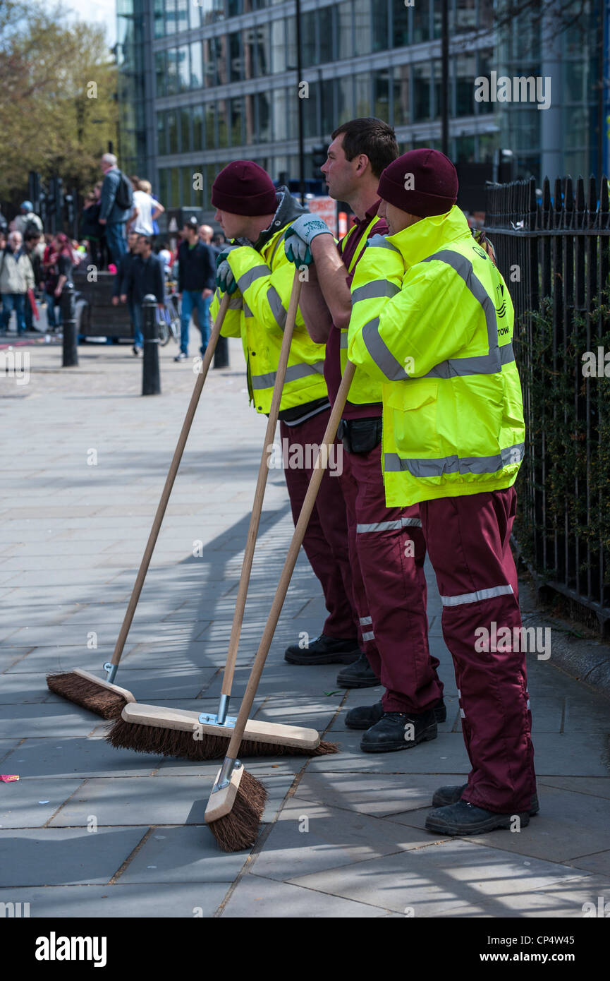 Three street cleaners in hi vis jackets leaning on their brooms at the ...