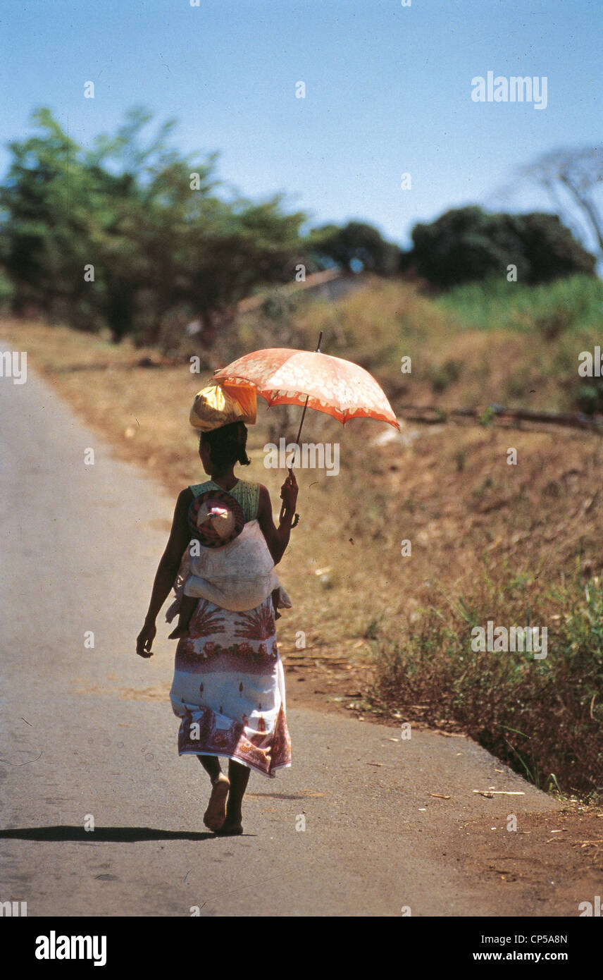 Madagascar - Nosy Be Island. Woman with child on her back and umbrella ...