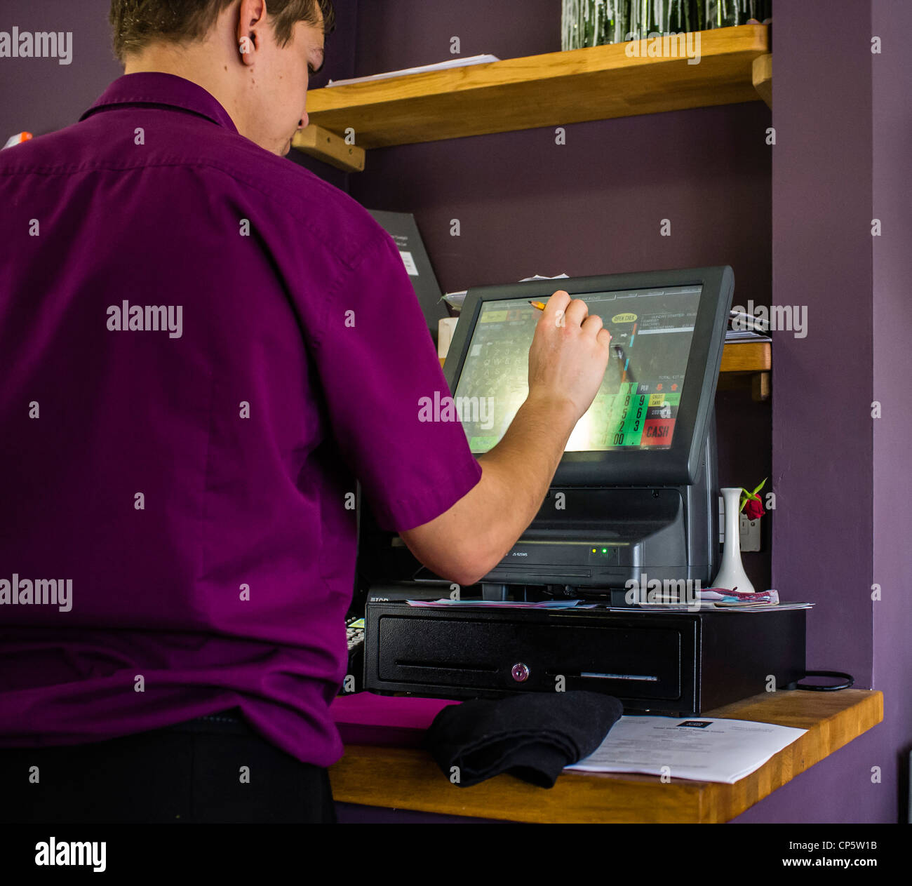 a young worker using a touch screen till to enter details of a meal in ...