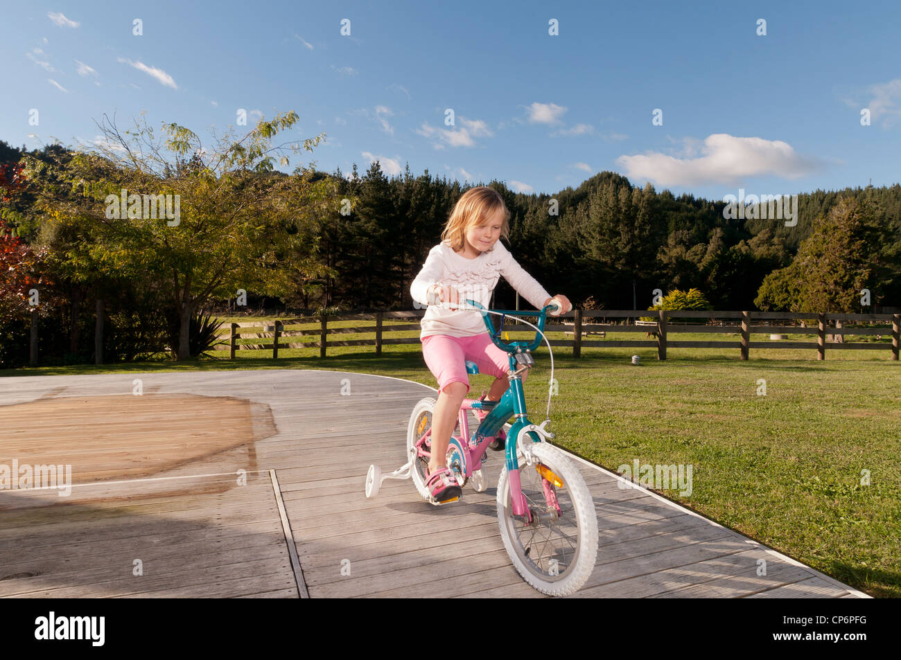 Girl riding here bike on wooden decking, New Zealand Stock Photo - Alamy