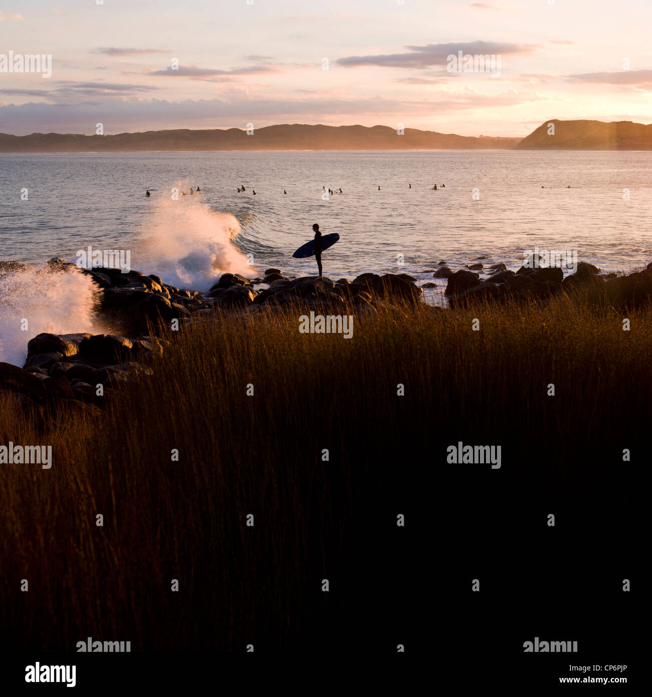 Manu Bay with surfers and surfer walking over rocks to enter the water ...