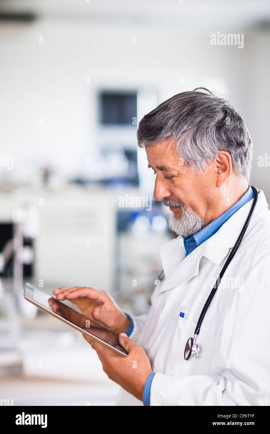 Senior doctor using his tablet computer at work (color toned image ...
