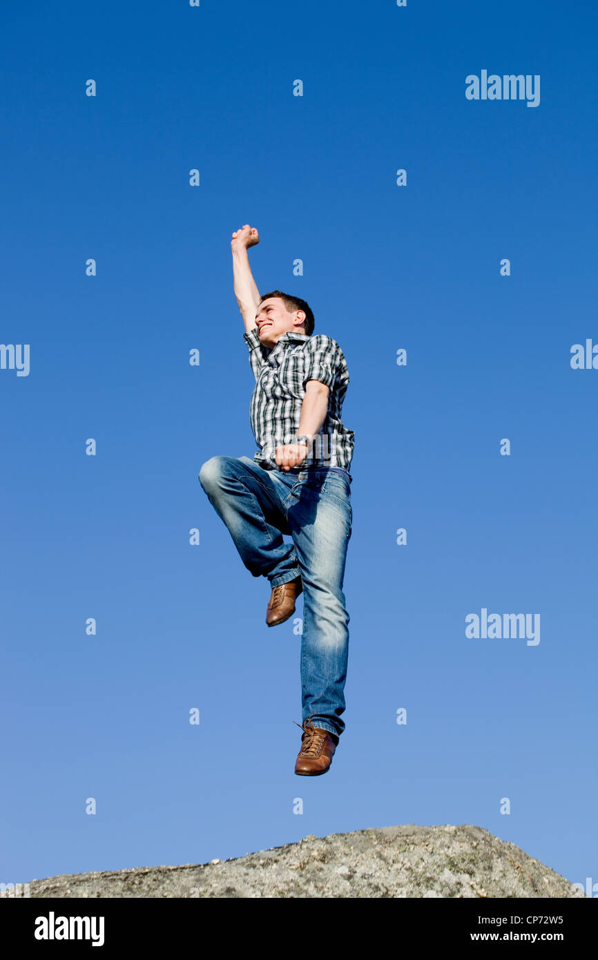 young happy man, with a big jump, on top of a rock Stock Photo - Alamy