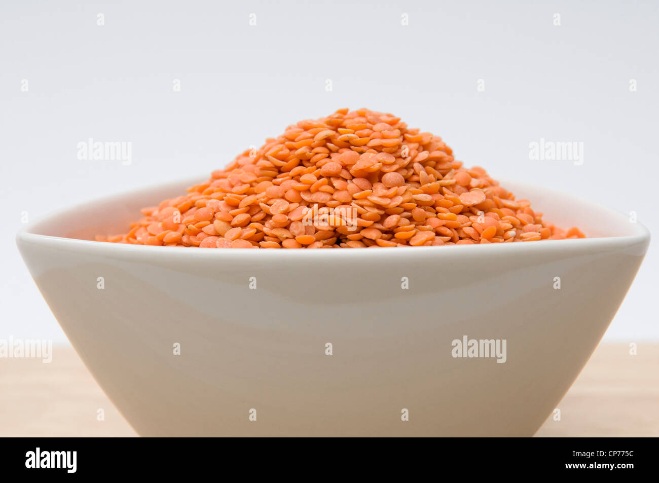 Dried red lentils in white bowl on wooden board against a white ...