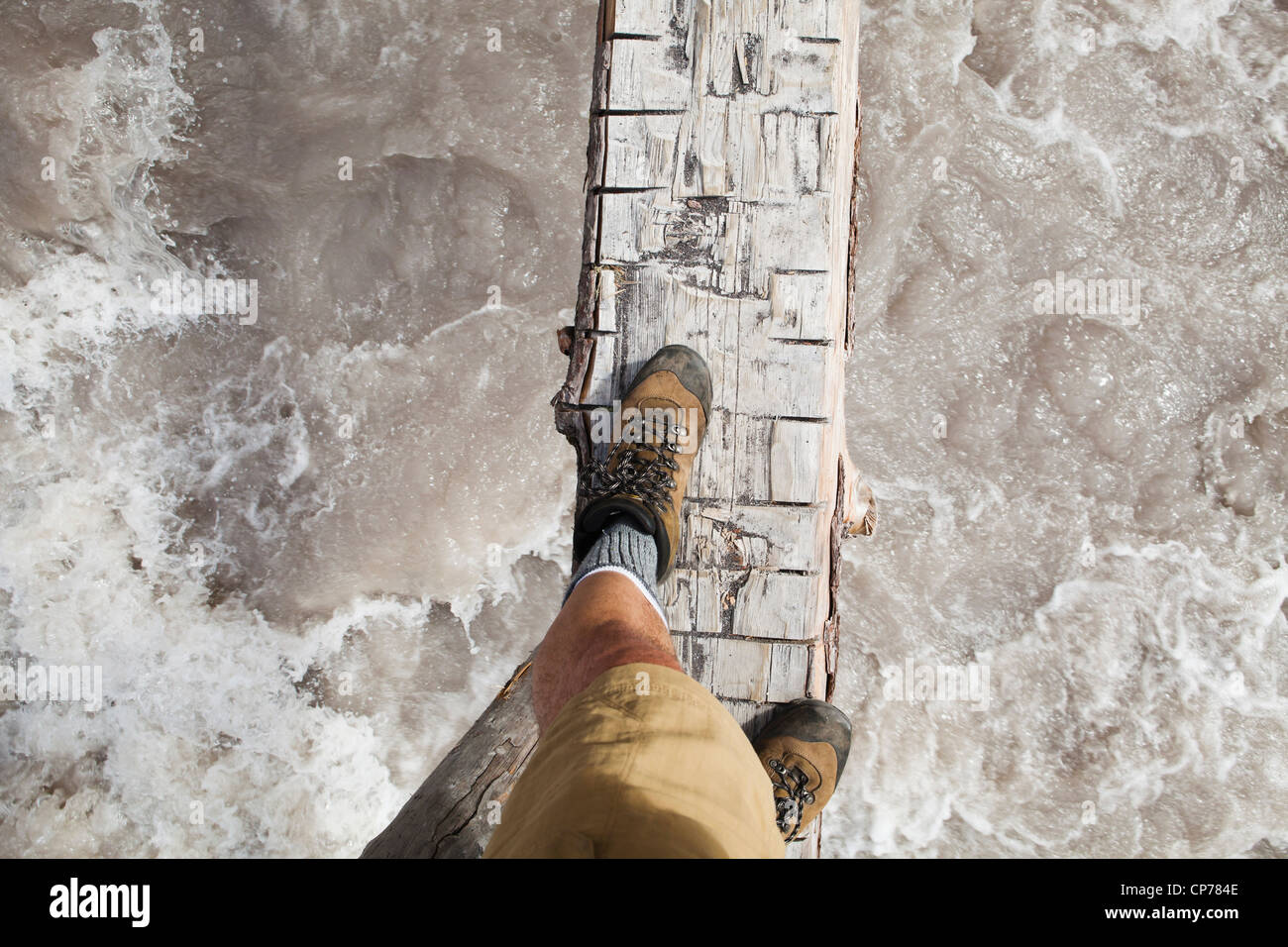 Looking down at feet on a narrow one log bridge over a roiling river ...