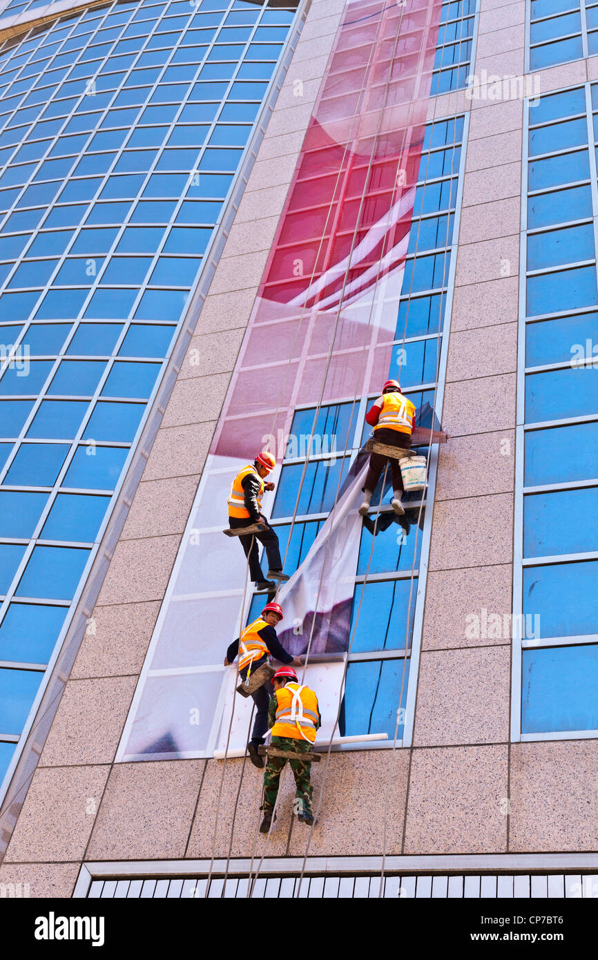Workmen hanging a poster or billboard in sections on the side of a ...