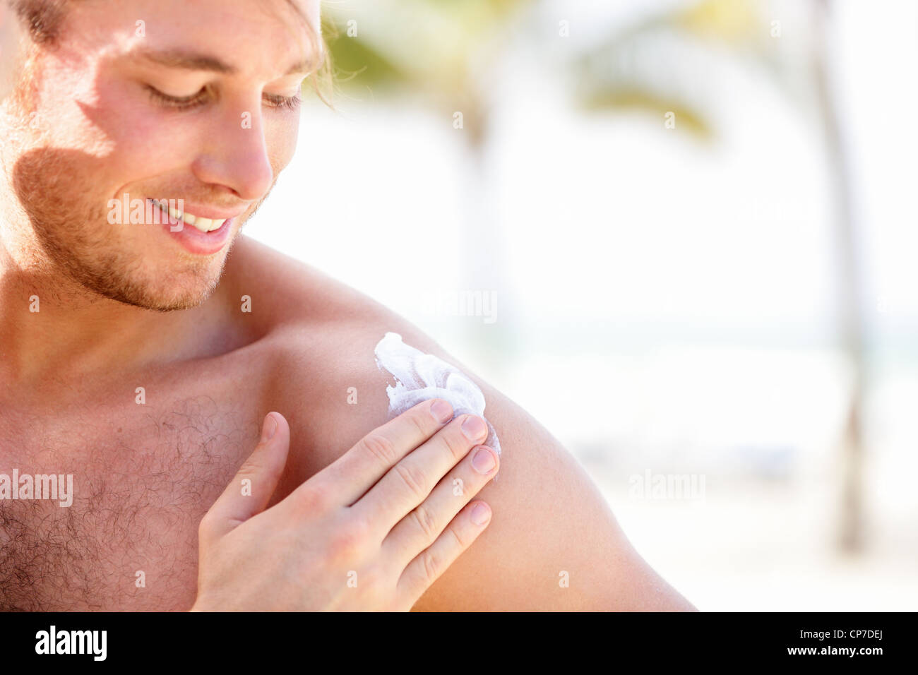 Happy young Caucasian male model putting sunblock sun screen cream on ...