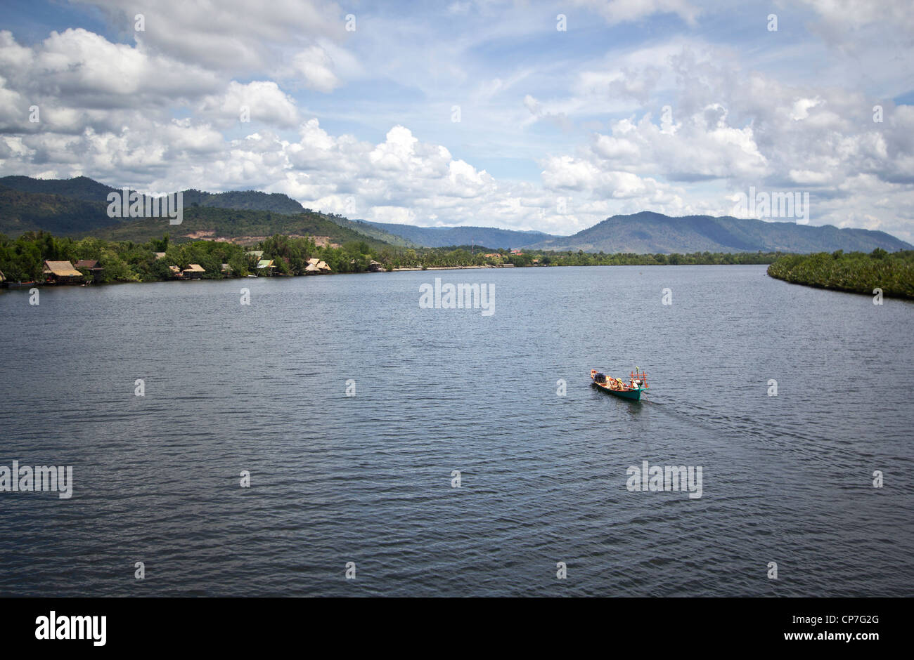 A fishing boat traveling up the Kampot River, with the Bokor Mountains ...