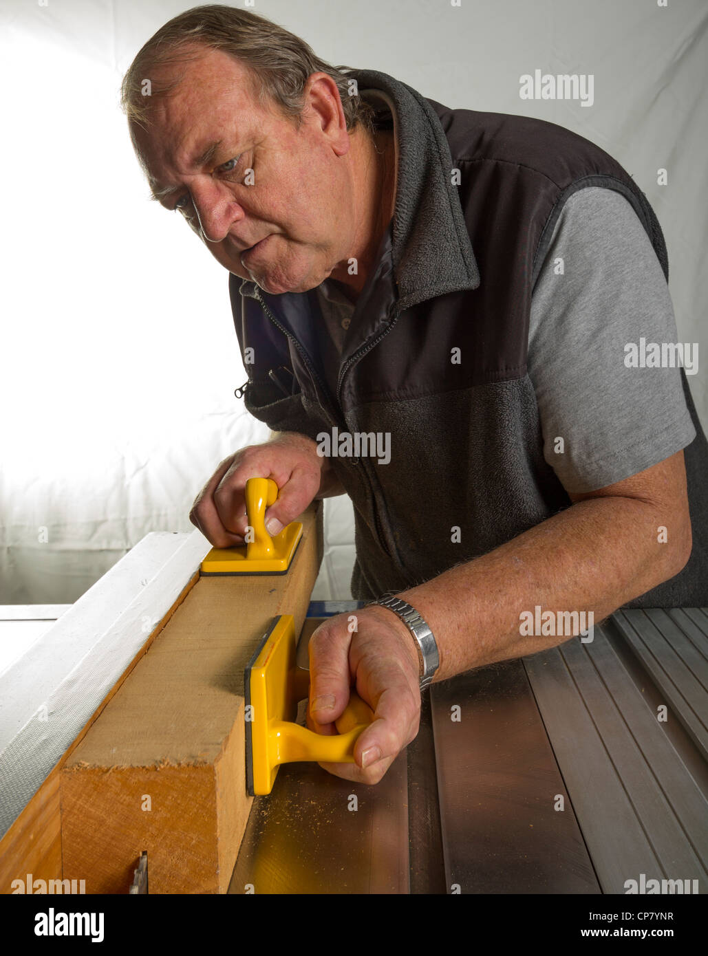Senior male woodworker guiding a piece of wood through a saw bench ...