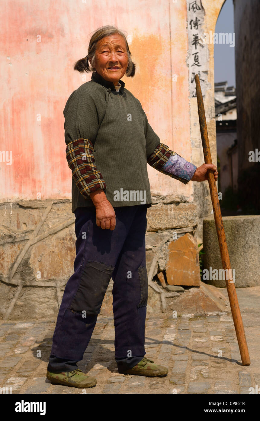Old Chinese woman with staff walking in ancient village of Chengkan ...