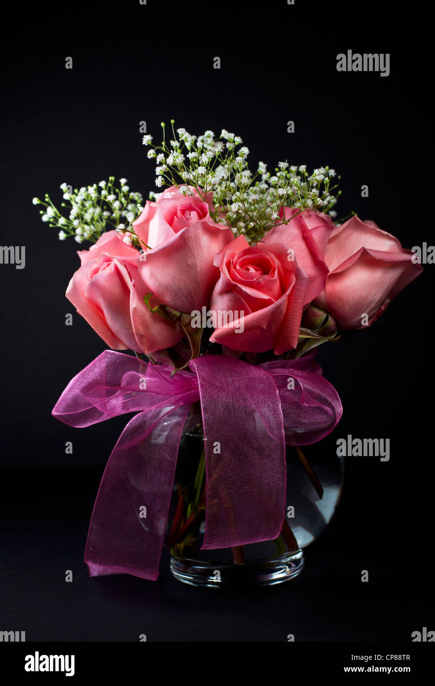 Pink roses with small white flowers in glass vase on dark background ...
