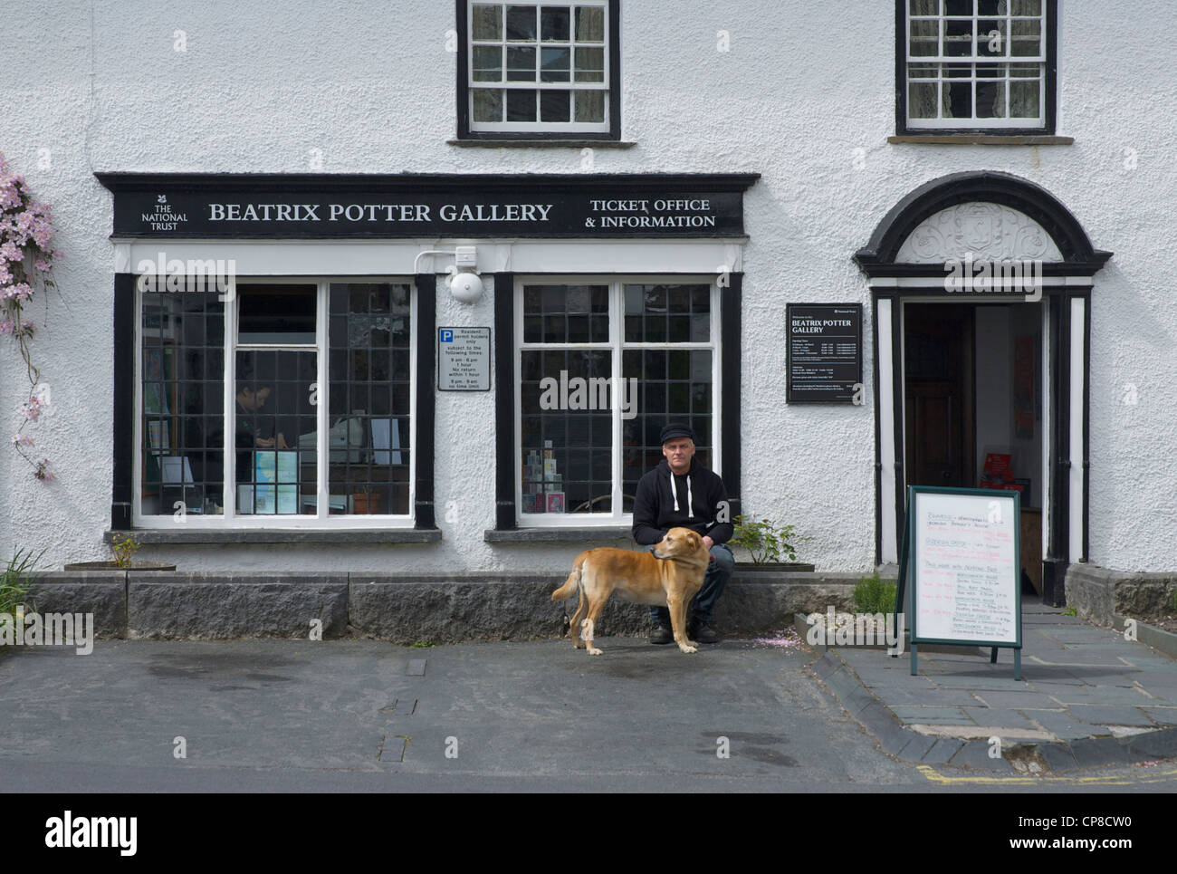Man and dog sitting outside the Beatrix Potter Gallery, in the village ...