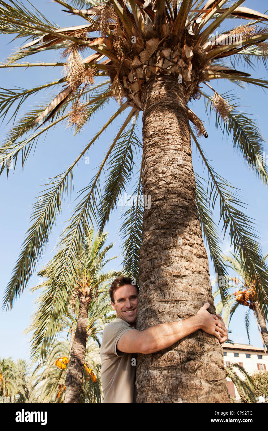 Spain, Mallorca, Palma, Mid adult man hugging palm tree, smiling Stock ...