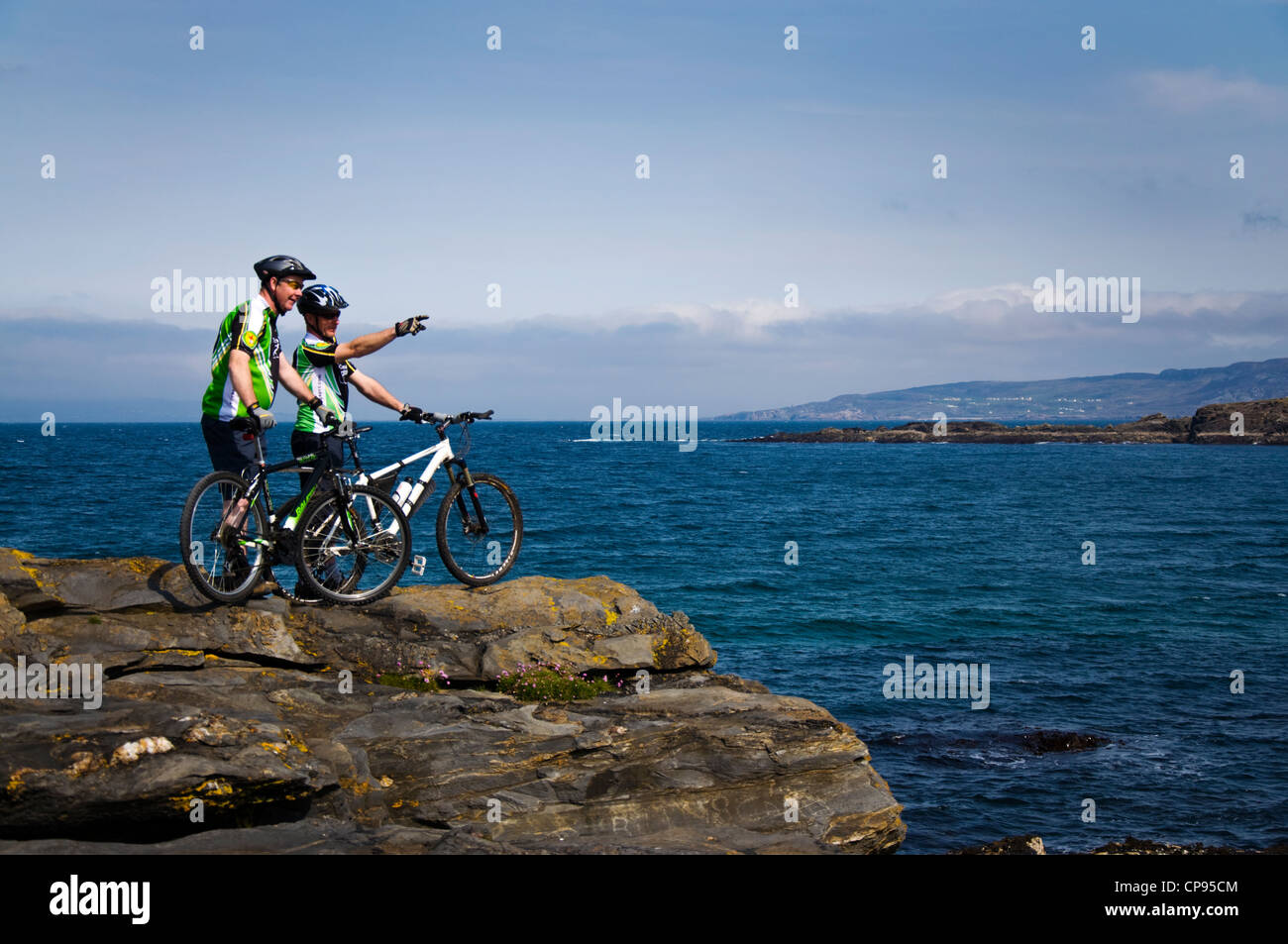 Cyclists with mountain bikes stand on rocks pointing by Atlantic Ocean ...