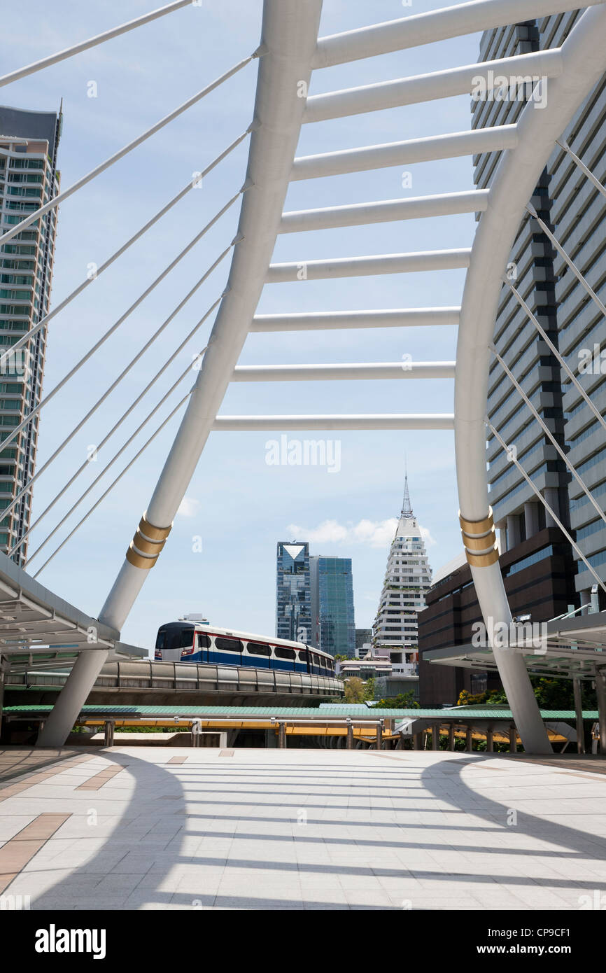 A mass transit train on an elevated track passes modern buildings in ...