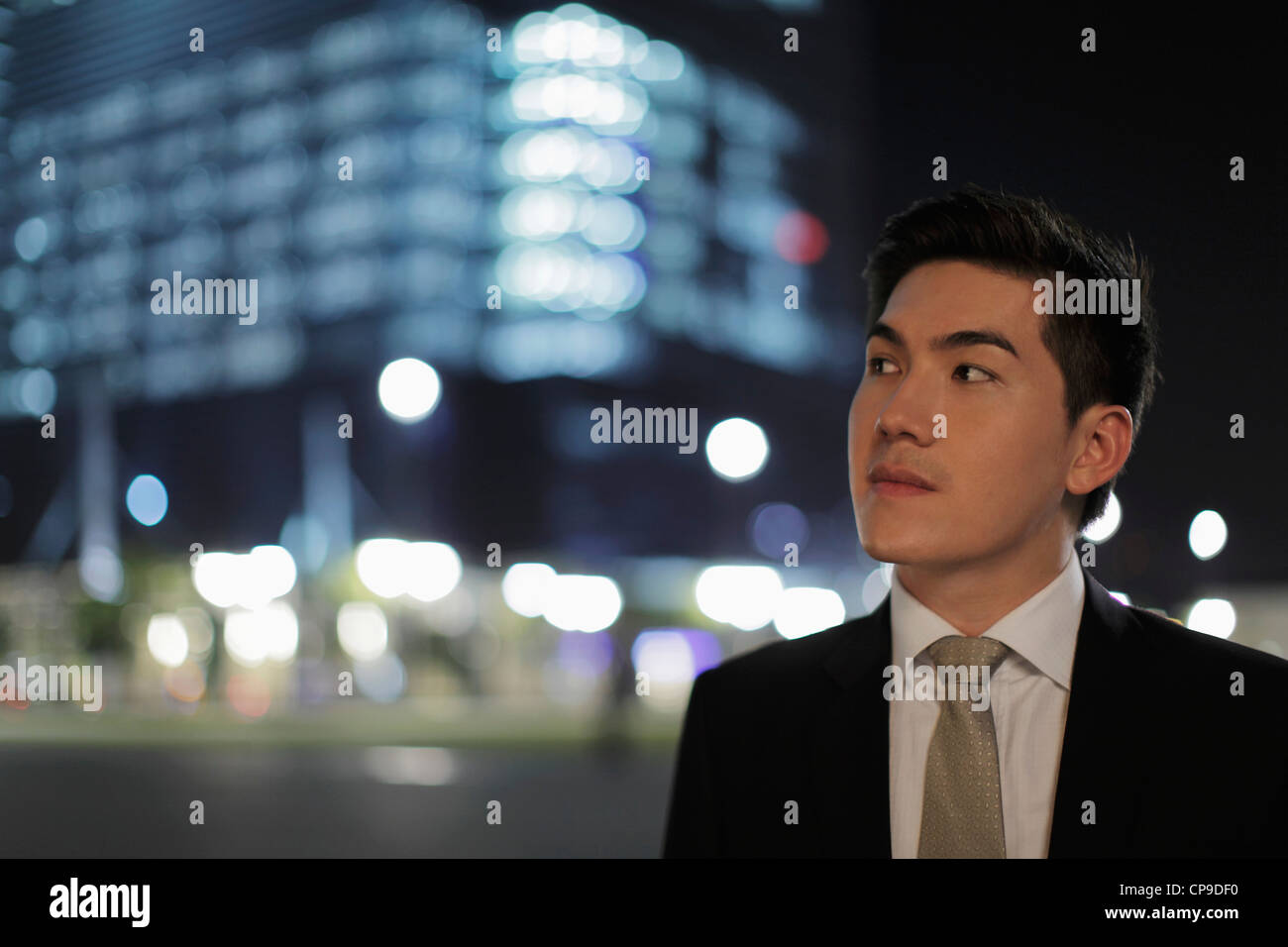 Man wearing a suit looking off, lit buildings in background Stock Photo ...