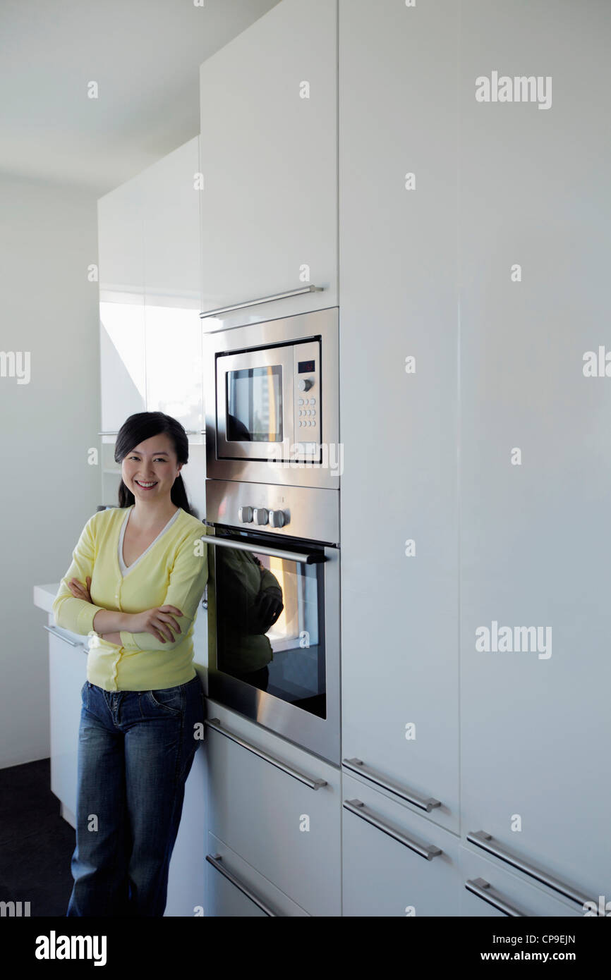 Young woman standing in her kitchen arms folded Stock Photo - Alamy