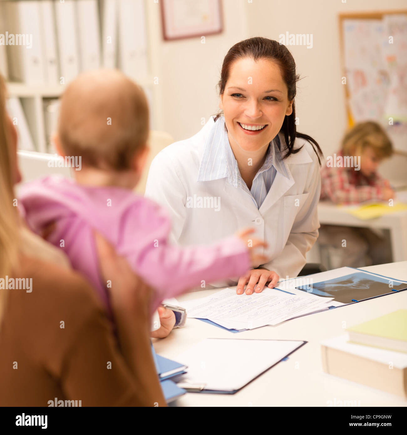 Female pediatrician smiling at baby patient sitting behind office desk ...