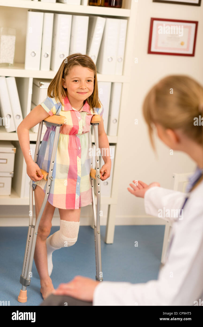 Little girl with bandaged leg standing with crutches surgery office ...