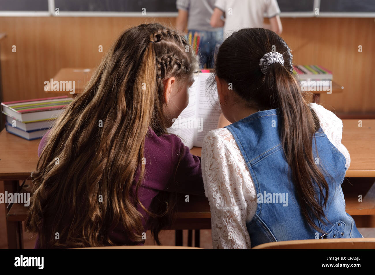 Two schoolgirls chatting in classroom during lesson Stock Photo - Alamy