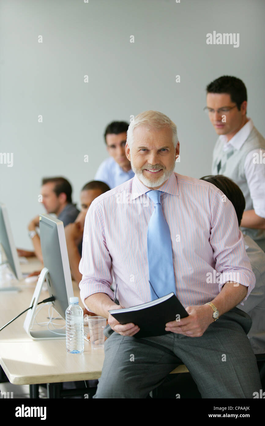 Senior manager sitting on a desk in front of his team Stock Photo - Alamy