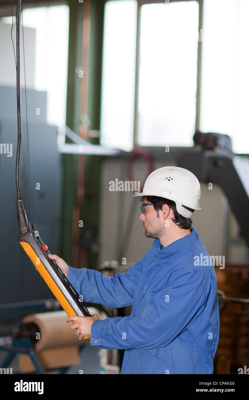 Blue collar worker using a crane in factory Stock Photo - Alamy