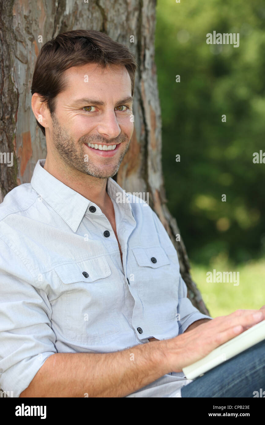 Young man sitting at the foot of a tree Stock Photo - Alamy
