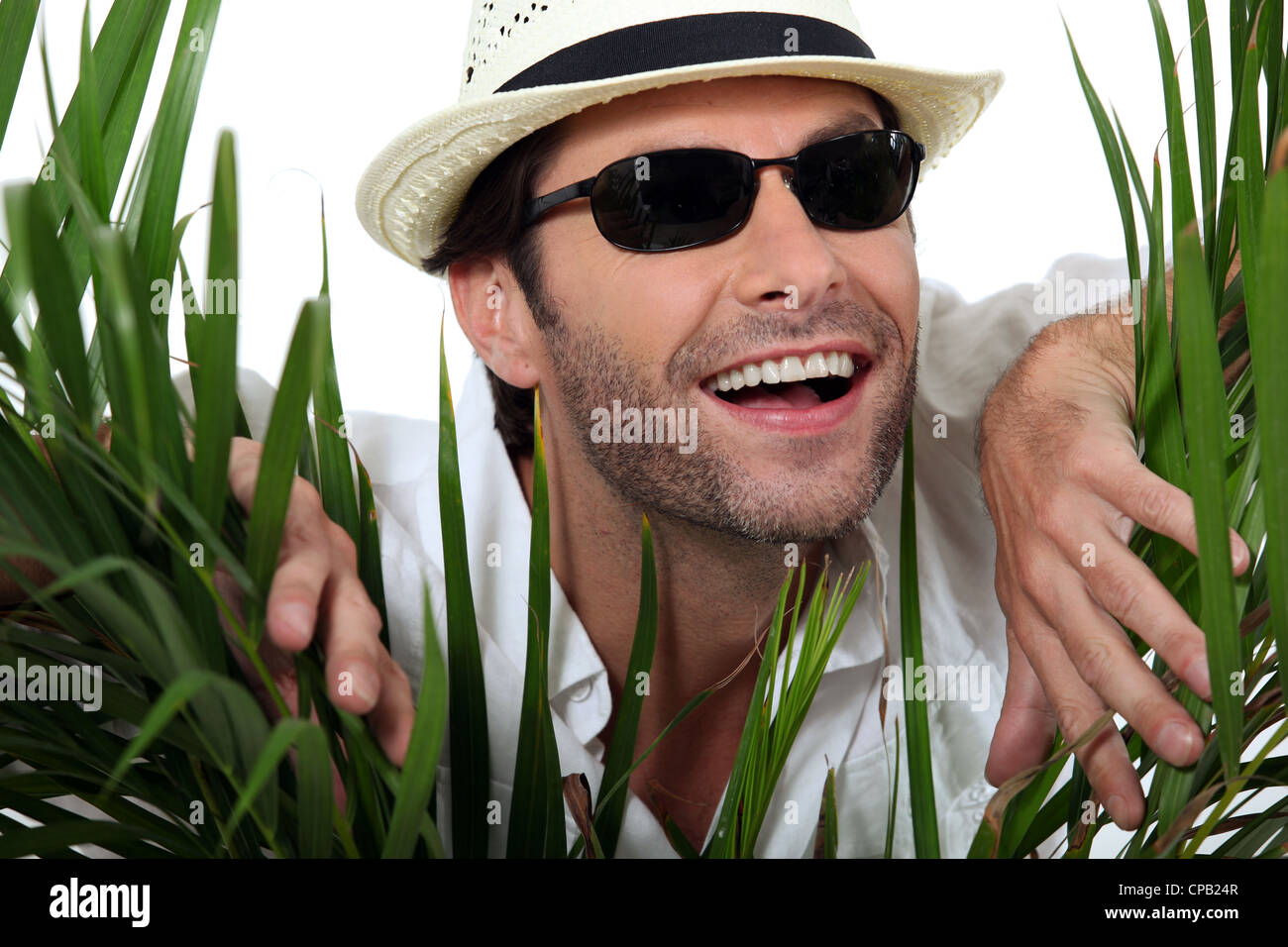 Man wearing hat behind bush Stock Photo - Alamy