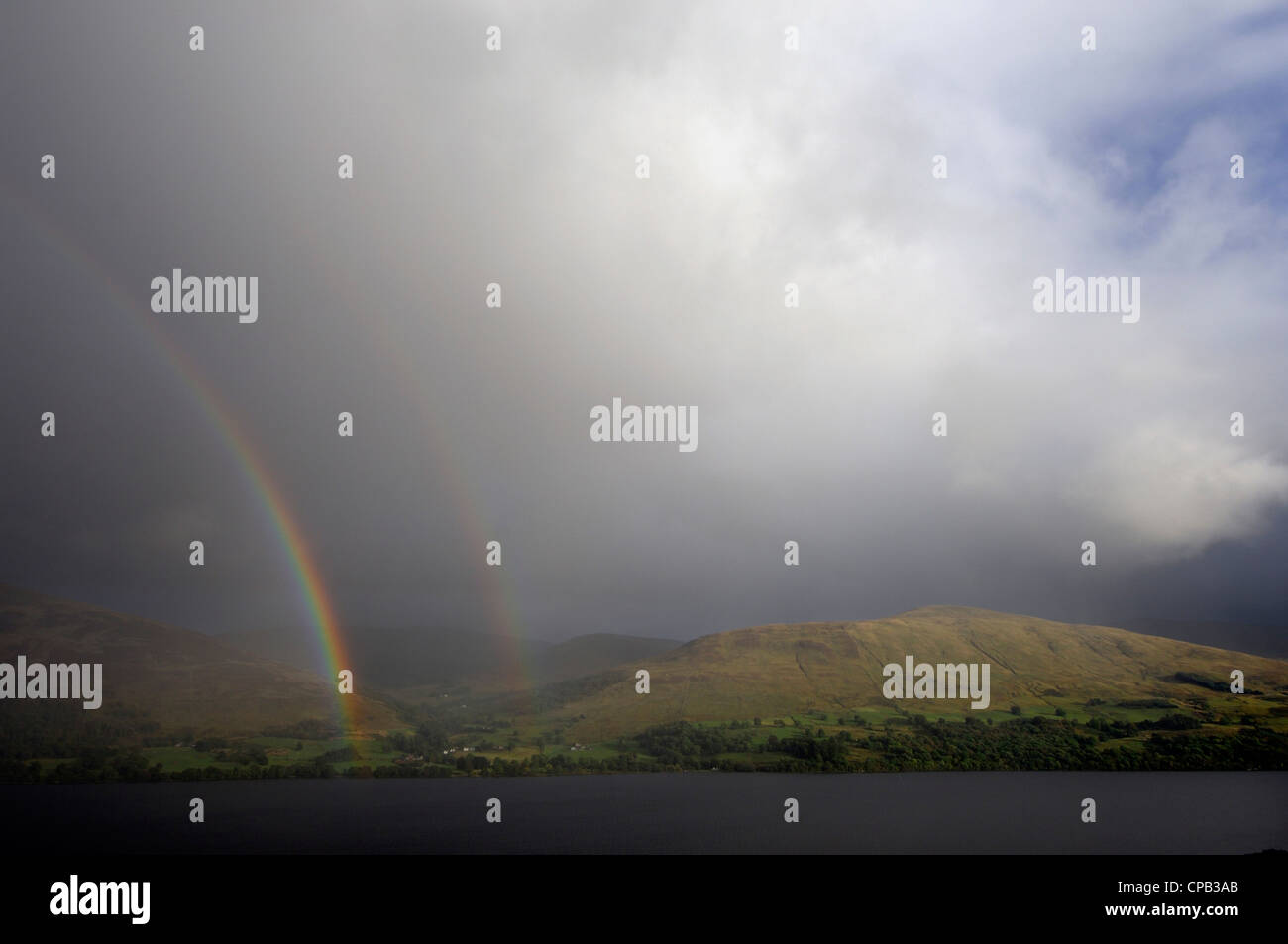 Bright rainbow with faint double against a dark-grey sky over Loch Tay ...