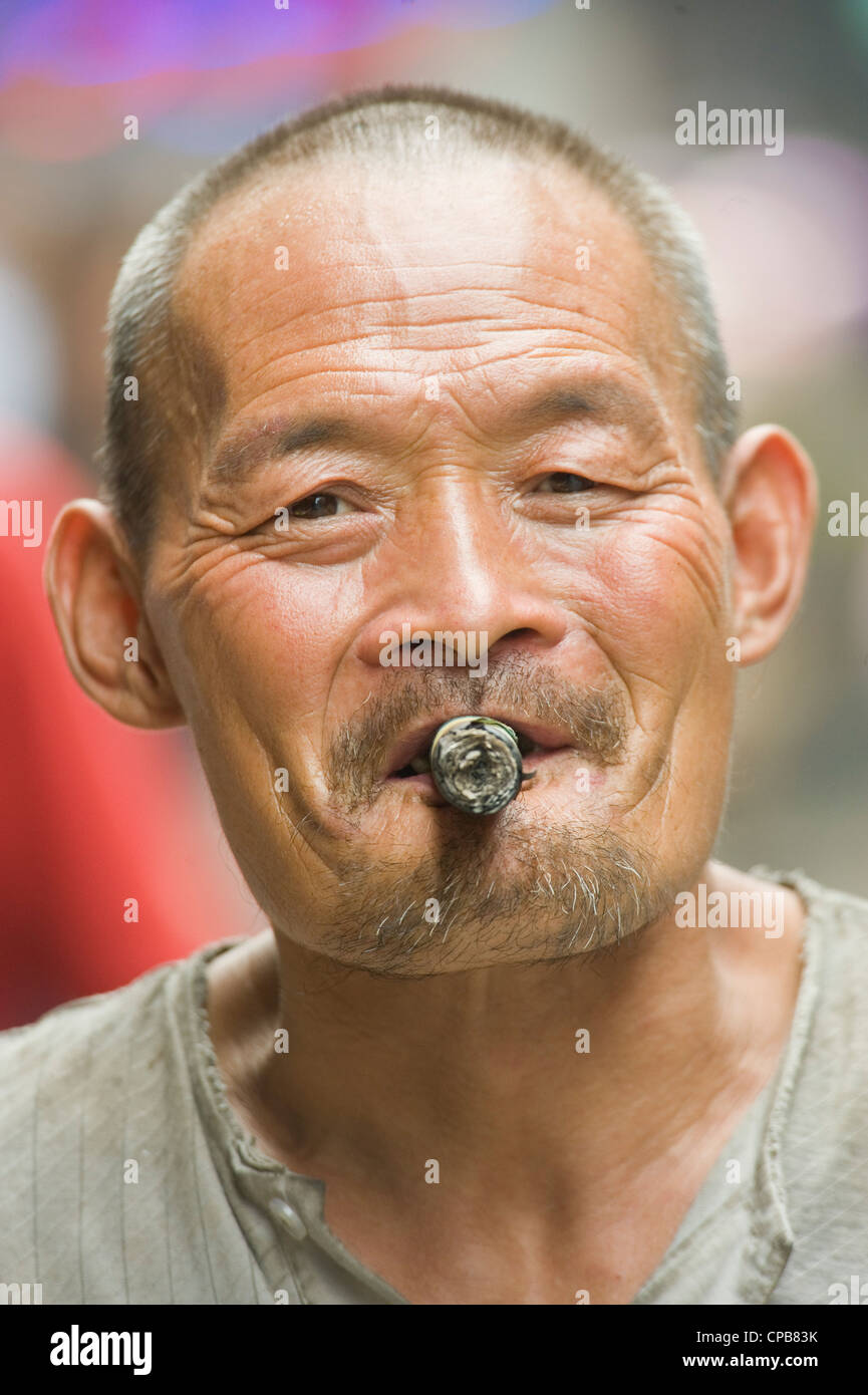 A friendly elderly Chinese man smoking a cigar poses for the camera ...
