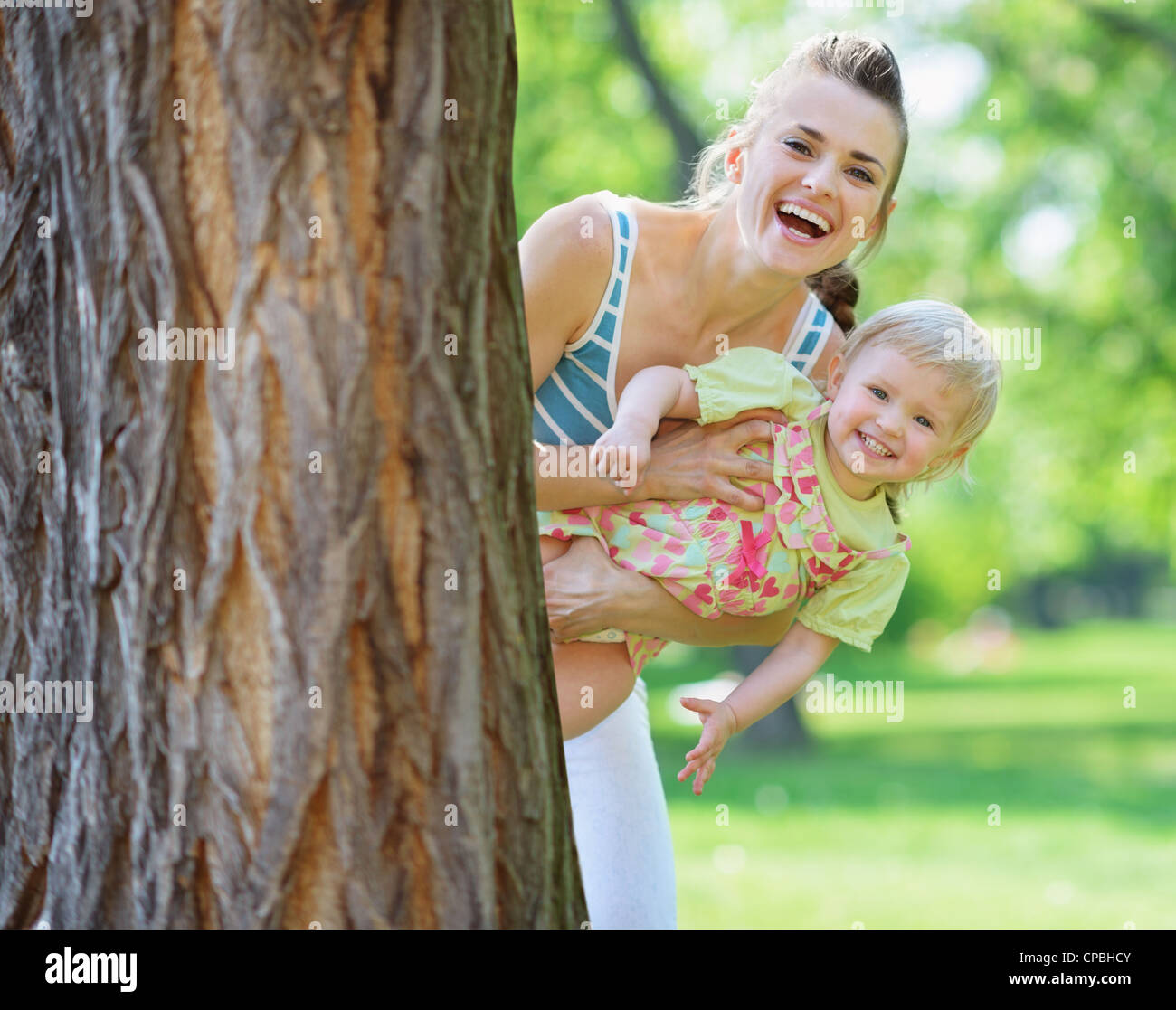 Smiling mother and baby looking out from tree Stock Photo - Alamy