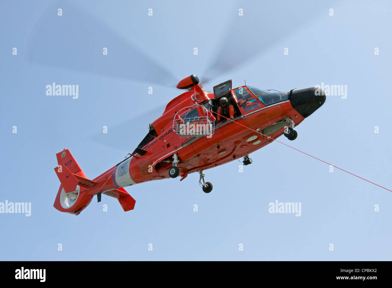 A United States Coast Guard HH-65C Dolphin helicopter lowers a rescue ...