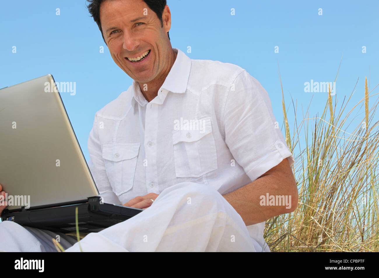 Man smiling on laptop in blue sky Stock Photo - Alamy