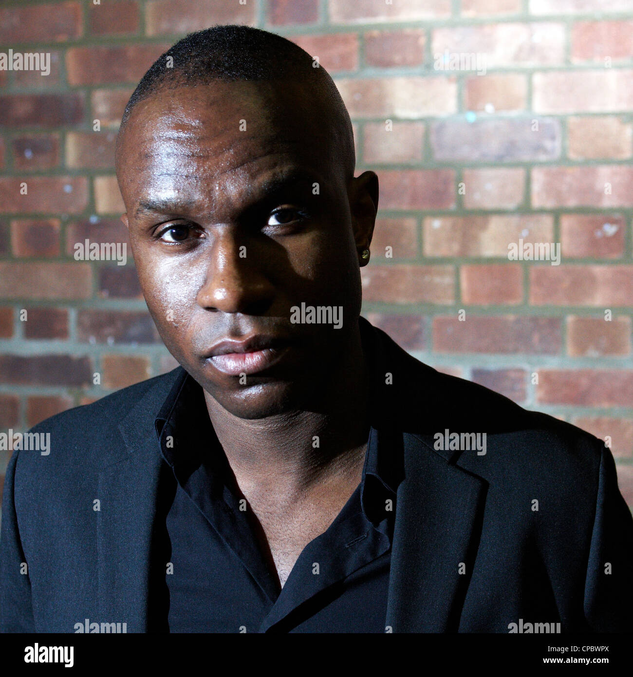 Portrait of a black man in a blue suit against a brick wall background ...