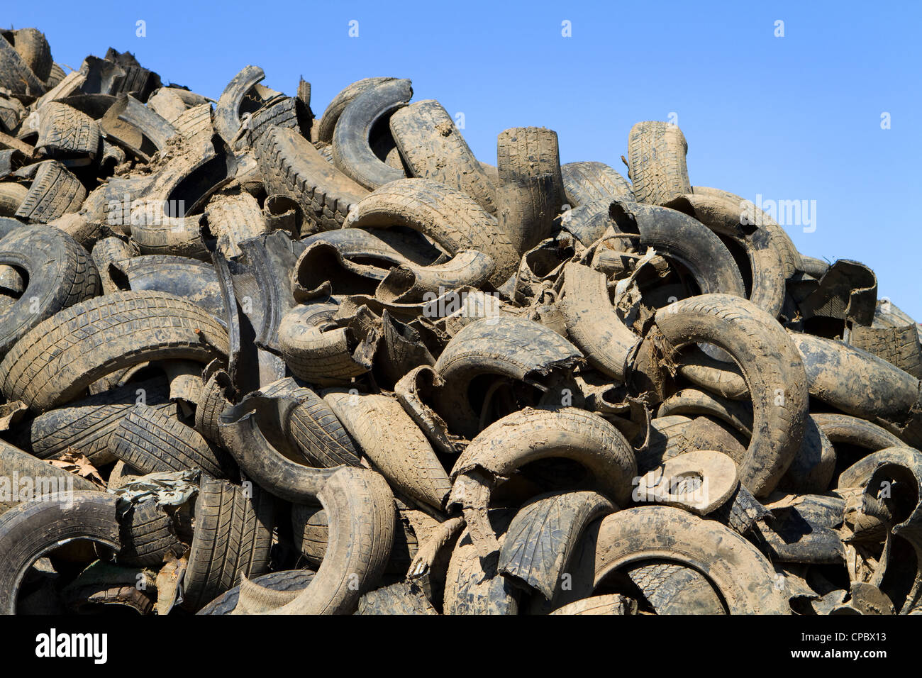 Heap of old muddy chopped up tires are piled in a recycling yard ...