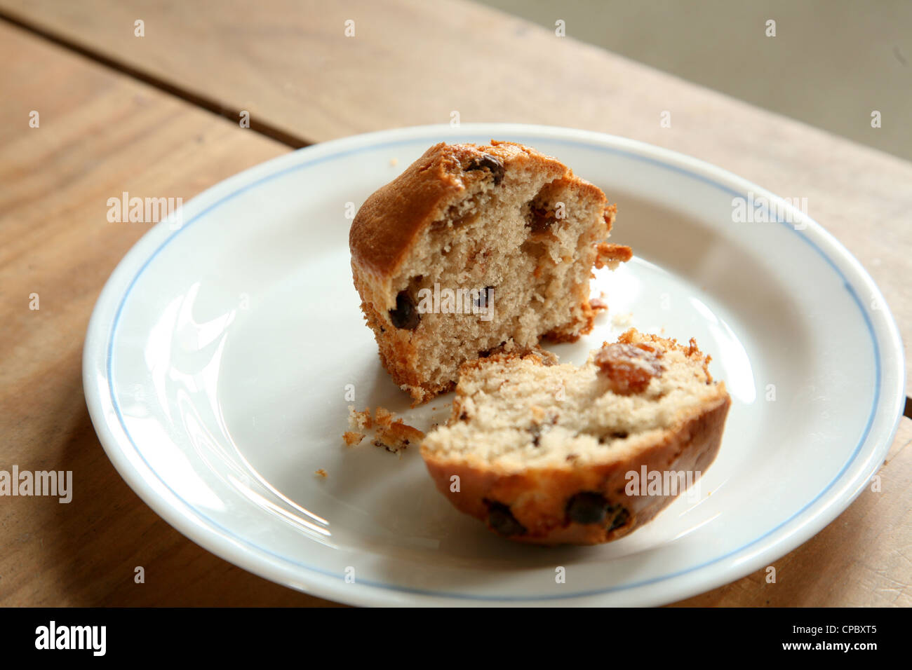 Fruit muffin sliced in half on a white plate on a wooden pine table ...