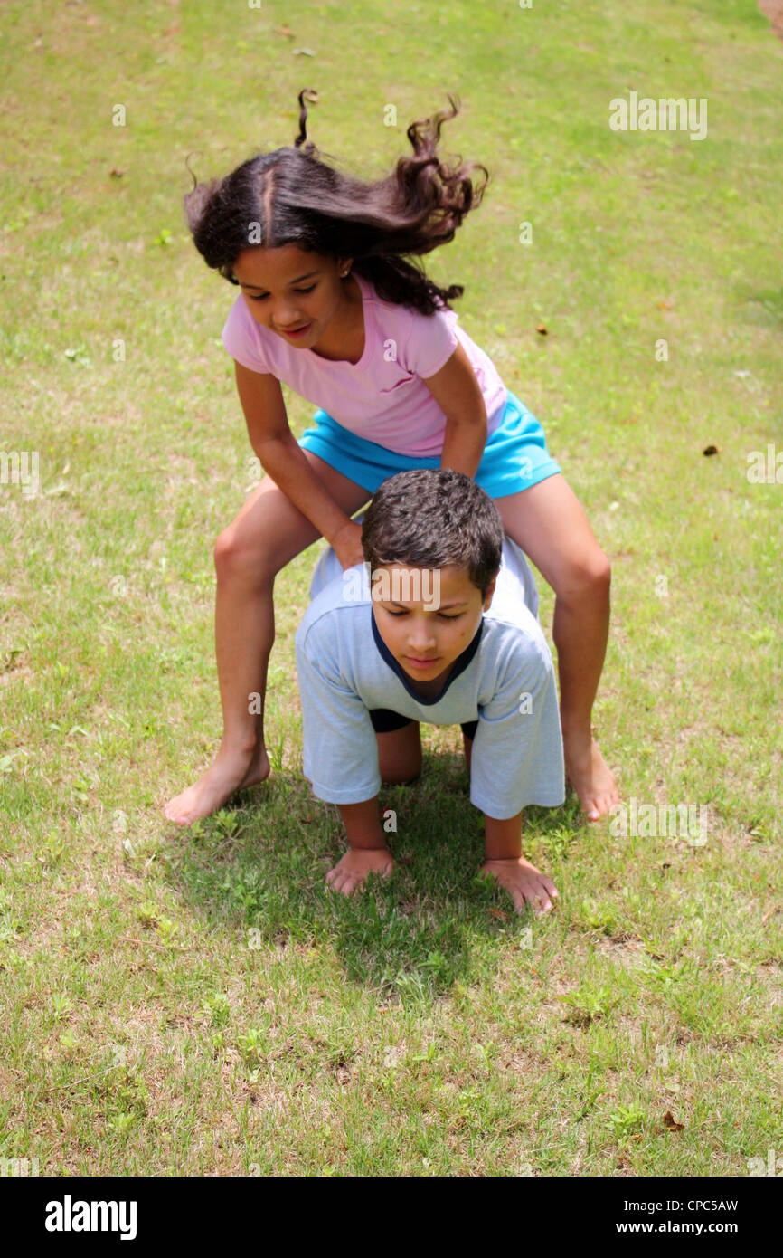 Girl and Boy playing leapfrog outside in the grass Stock Photo - Alamy