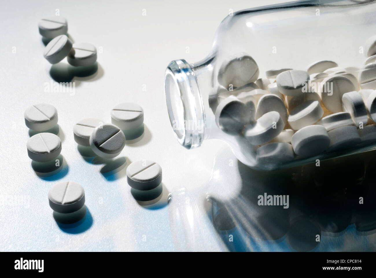 Glass with tablets on a reflecting surface. Some tablets lie outside ...