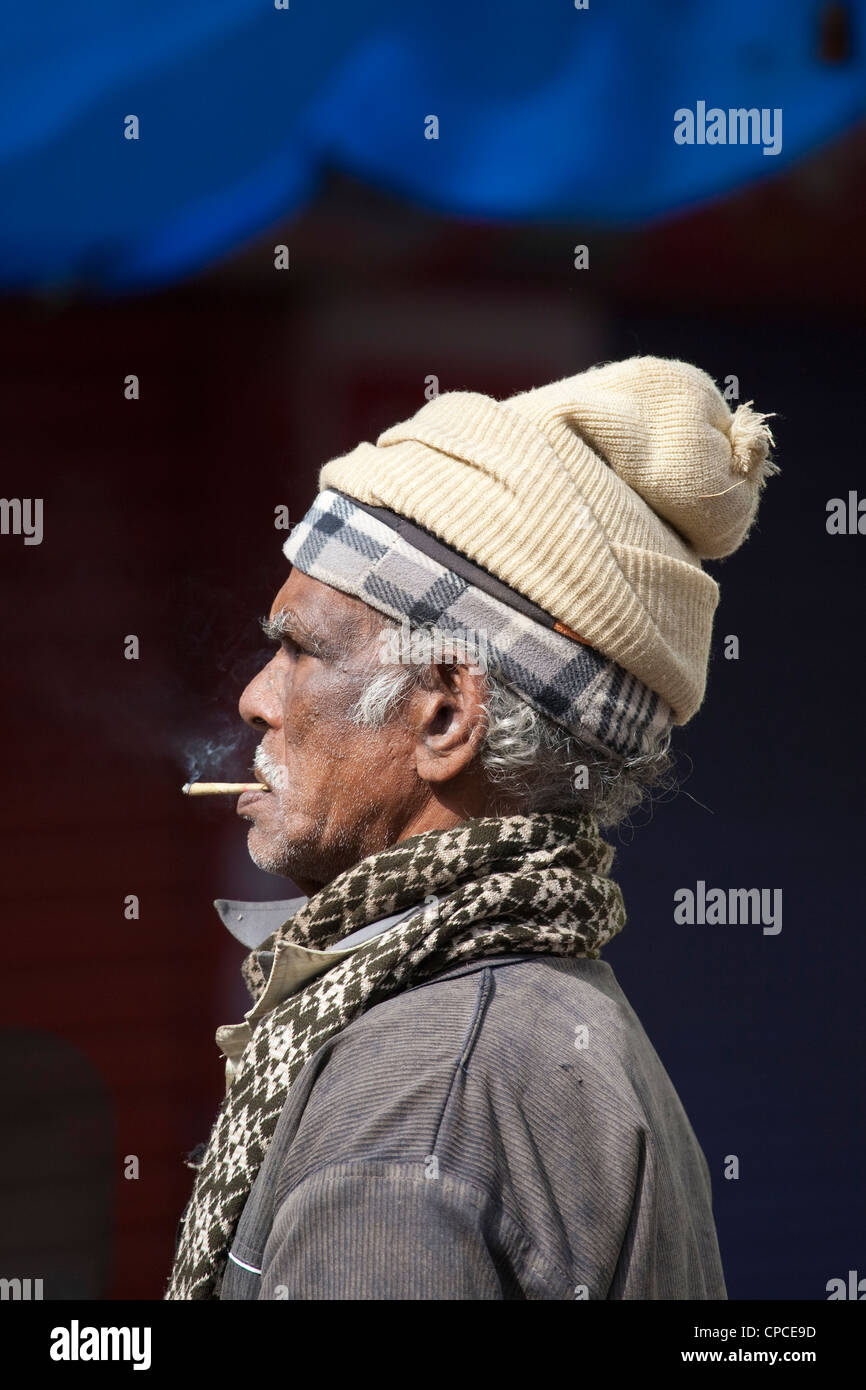 An Asian Indian man dressed for the cold and smoking on dark background ...