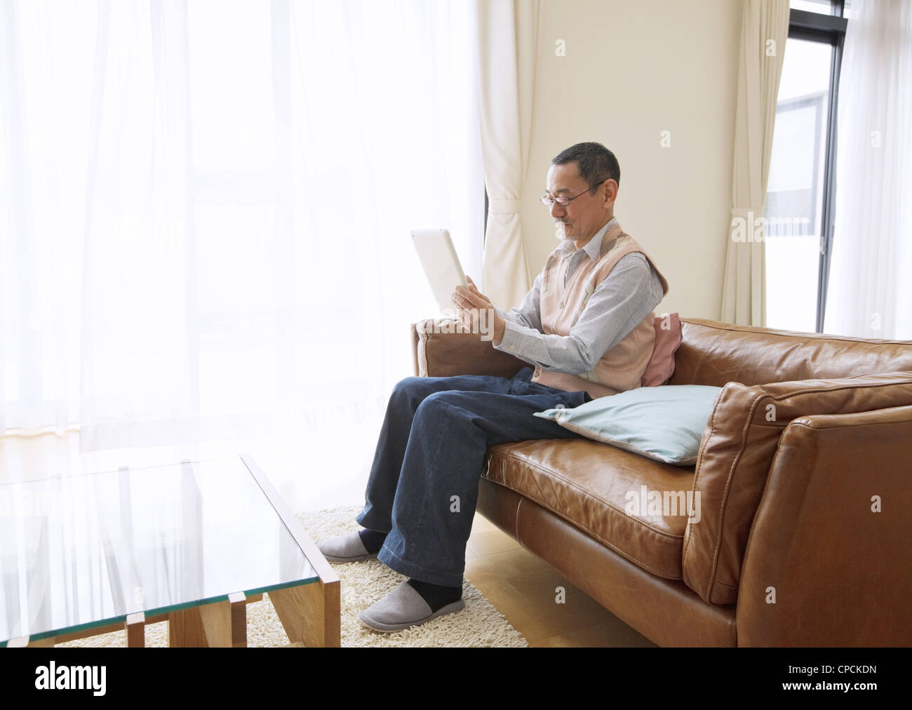 Senior man using tablet PC on a sofa Stock Photo - Alamy