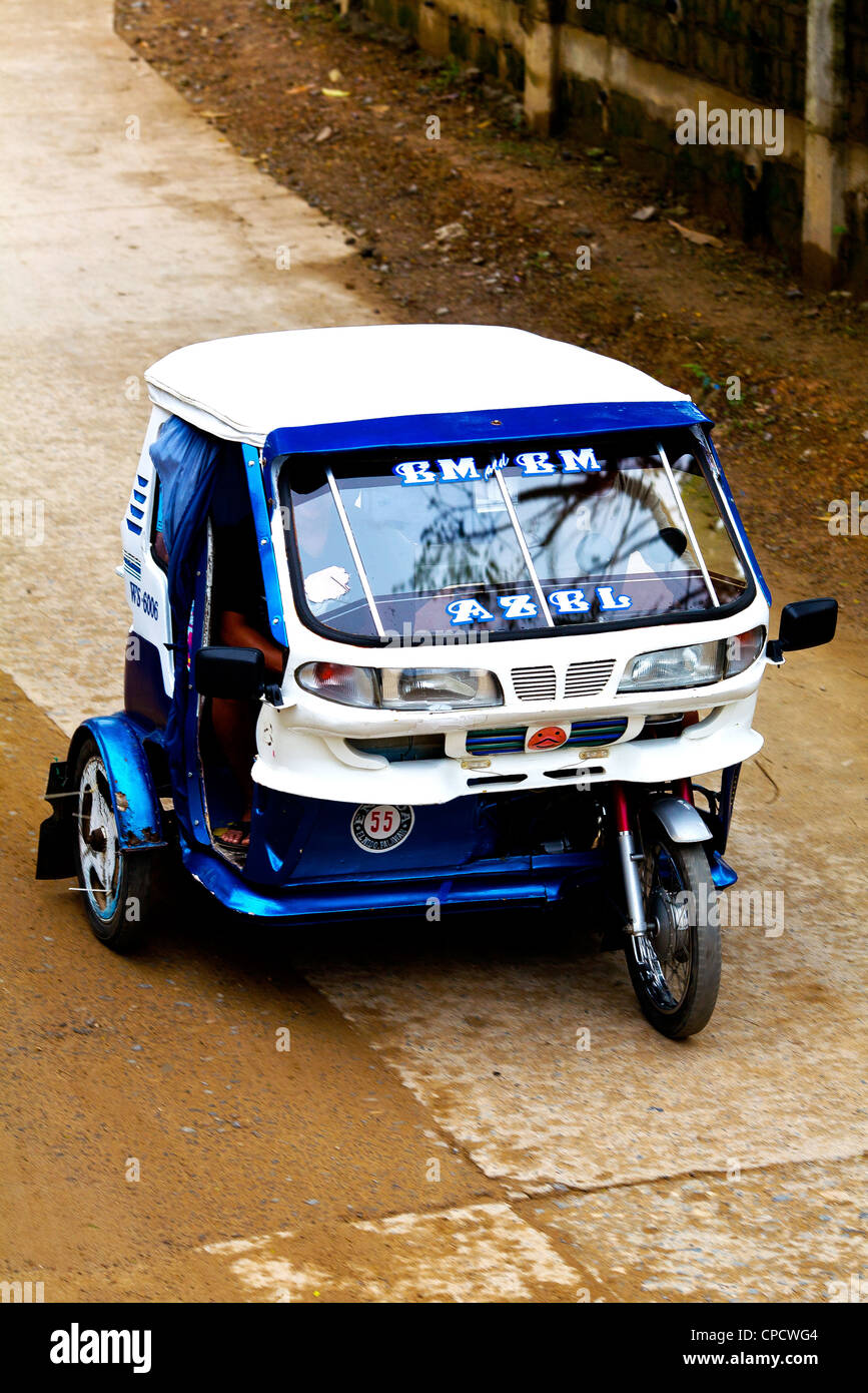 A blue and white tricycle taxi speeds down the main street of the town ...