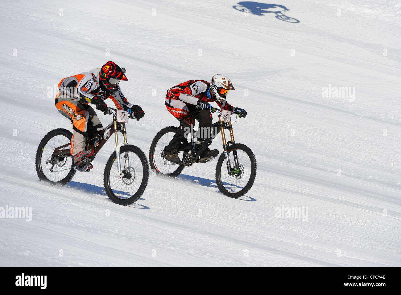 Two downhill mountain bikers go head-to-head racing at speed on snow ...
